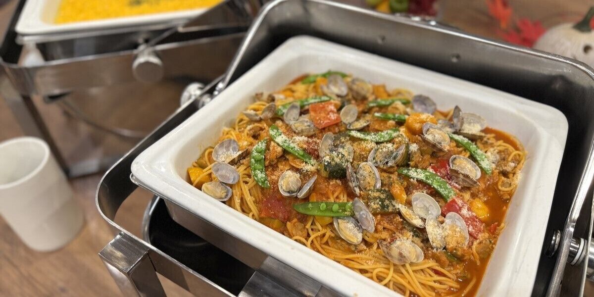 Buffet com prato de massa coberto com amêijoas e vegetais.