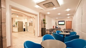 Um saguão de hotel moderno com cadeiras azuis, uma tela de televisão e uma área de recepção.