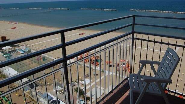 Varanda com vista para uma praia, área de piscina e uma cadeira.