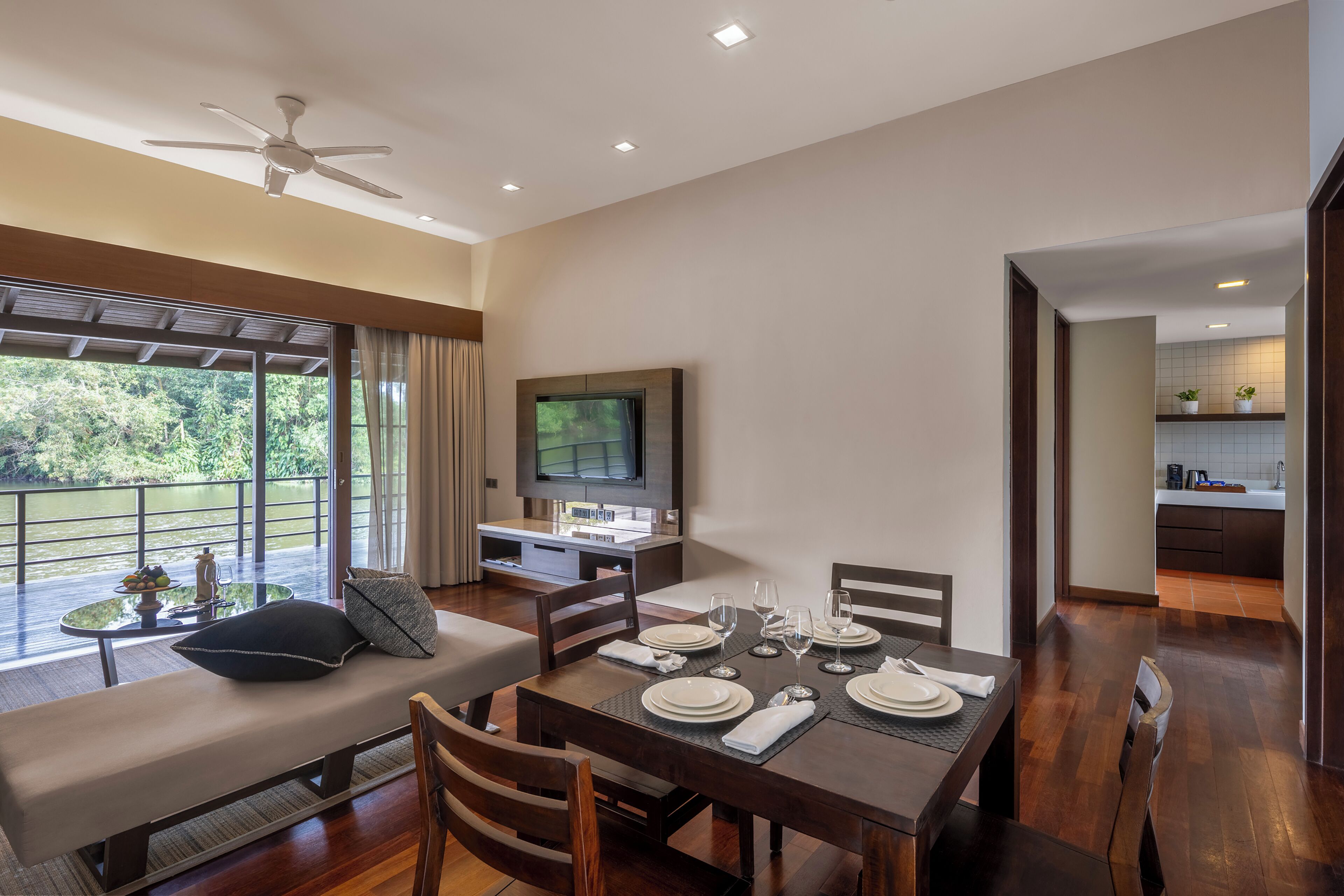 Uma sala de jantar moderna com mesa posta para quatro pessoas, um sofá com vista e uma televisão na parede.