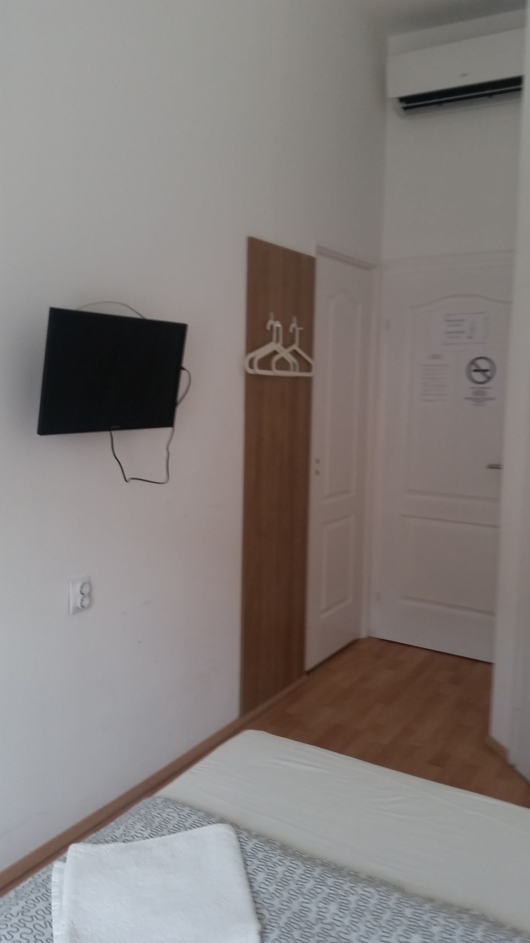 Quarto com televisão de tela plana fixada na parede, uma porta de madeira e uma porta branca com um aviso.