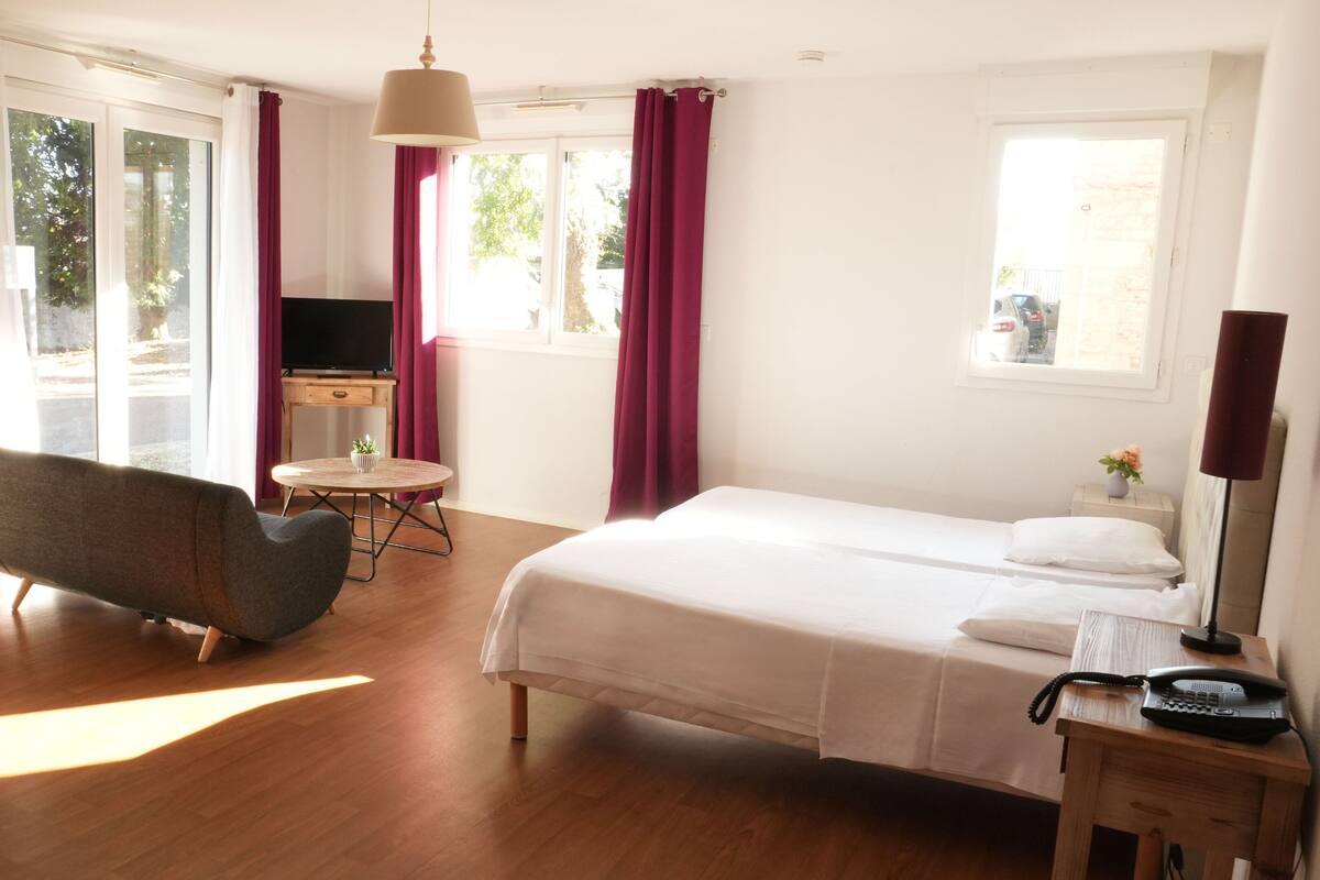 Quarto de hotel com cama, escrivaninha com luminária, cadeira e televisão.