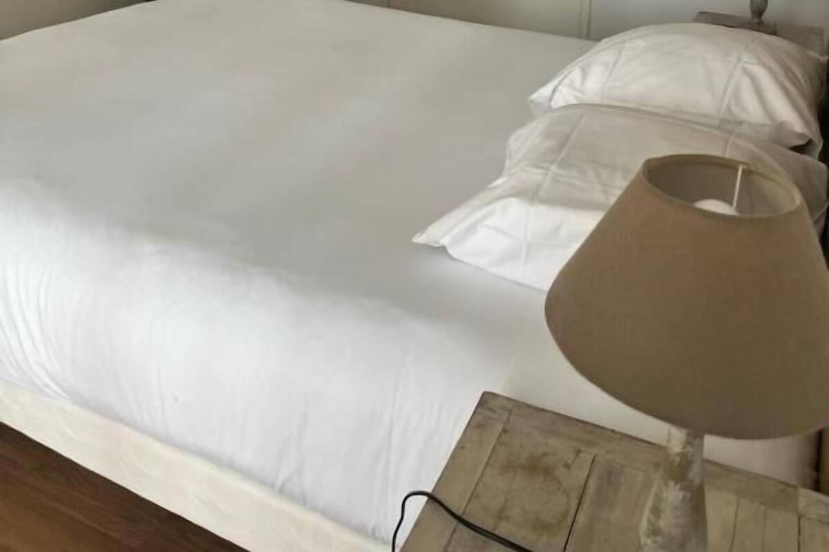 Quarto com cama, televisão sobre suporte, porta e abajur em mesa de cabeceira.