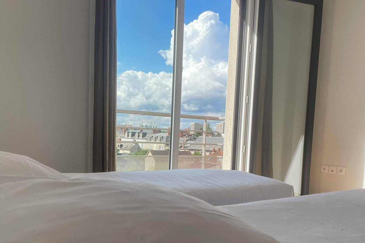 Quarto de hotel com duas camas, uma janela grande e vista para a cidade.