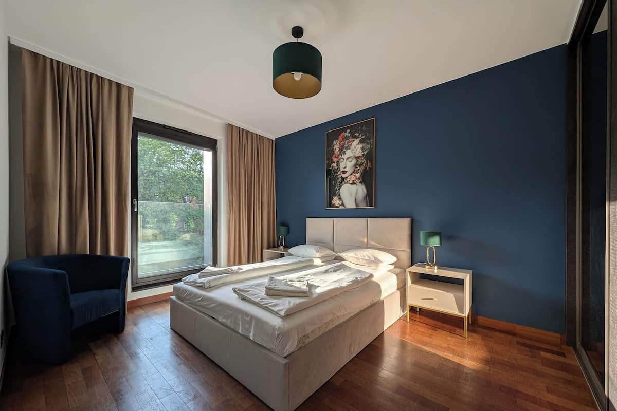 Quarto moderno com uma cama grande, uma cadeira, uma mesinha de cabeceira e um quadro na parede.