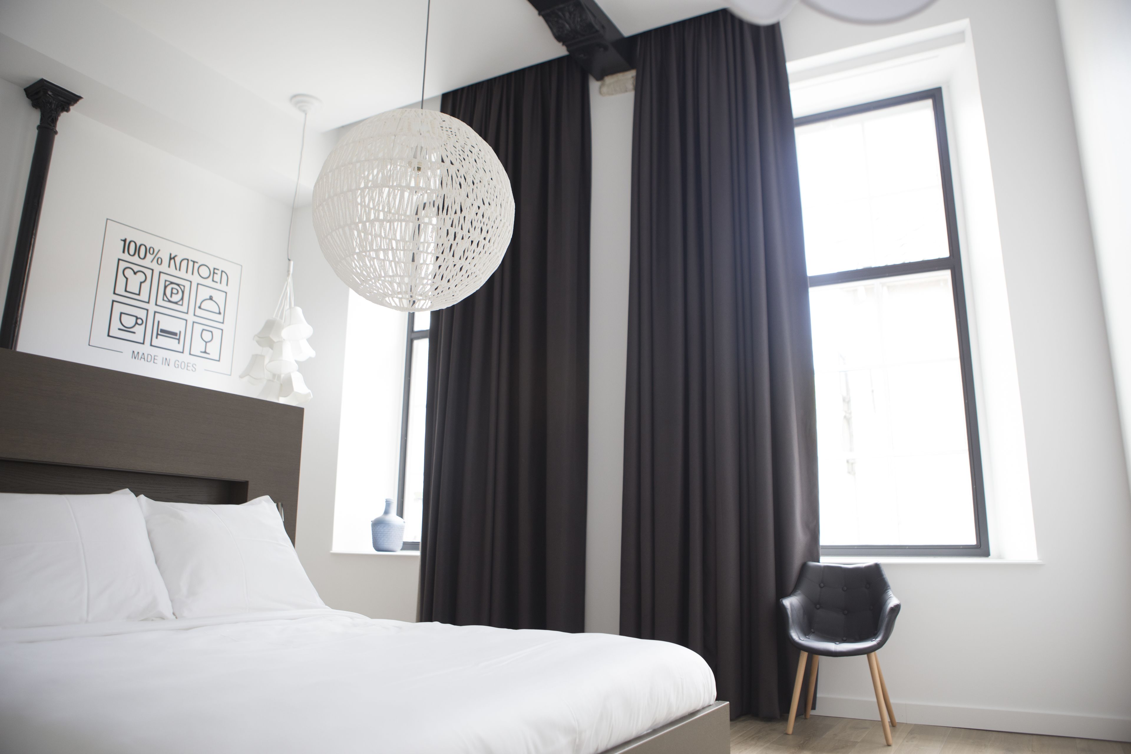 Quarto moderno com cama grande, luminária pendente e janela com cortinas.