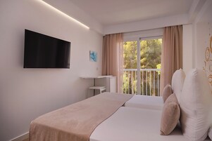 Quarto de hotel com cama, televisão de tela plana, janela com cortinas e vista para árvores.
