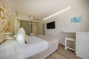 Quarto de hotel com cama, mesa de cabeceira e televisão na parede.