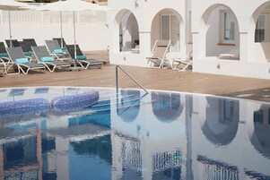Piscina com espreguiçadeiras e guarda-sóis, cercada por paredes brancas com arcos.