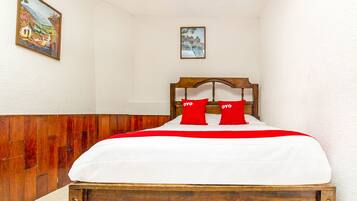 Cama bem arrumada com cabeceira de madeira, roupa de cama branca e duas almofadas vermelhas com a inscrição 'OYO'.