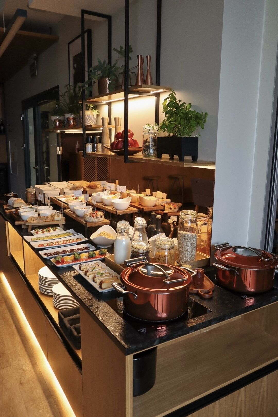 Disposição de buffet com diversos alimentos e recipientes, incluindo potes e tigelas, sobre um balcão de madeira com design moderno.