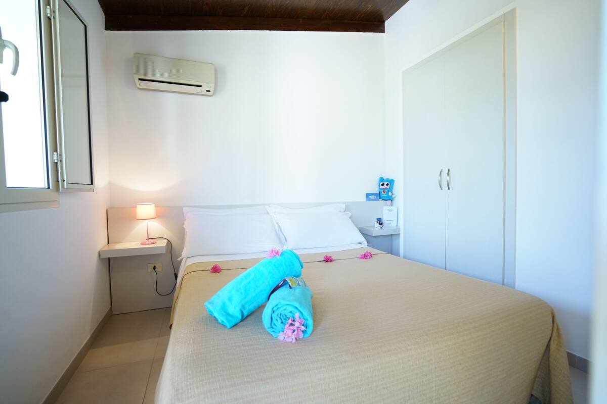 Quarto de hotel com cama, mesa de cabeceira, abajur, ar condicionado e guarda-roupa.