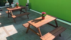 Uma área de pátio ao ar livre com mesas de piquenique de madeira e plantas em vasos.