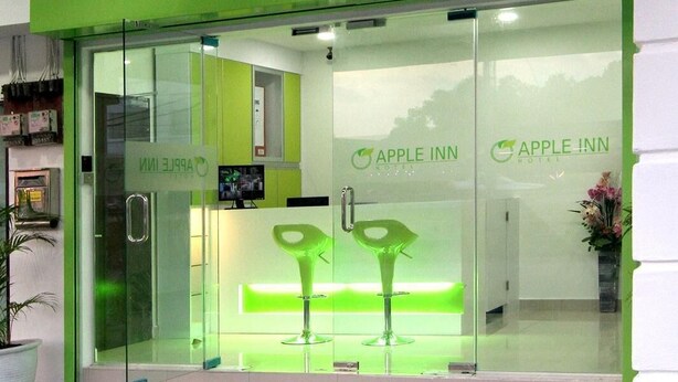 Exterior do Hotel Apple Inn, com fachada verde, dois bancos altos no interior e uma placa indicando o nome do hotel.