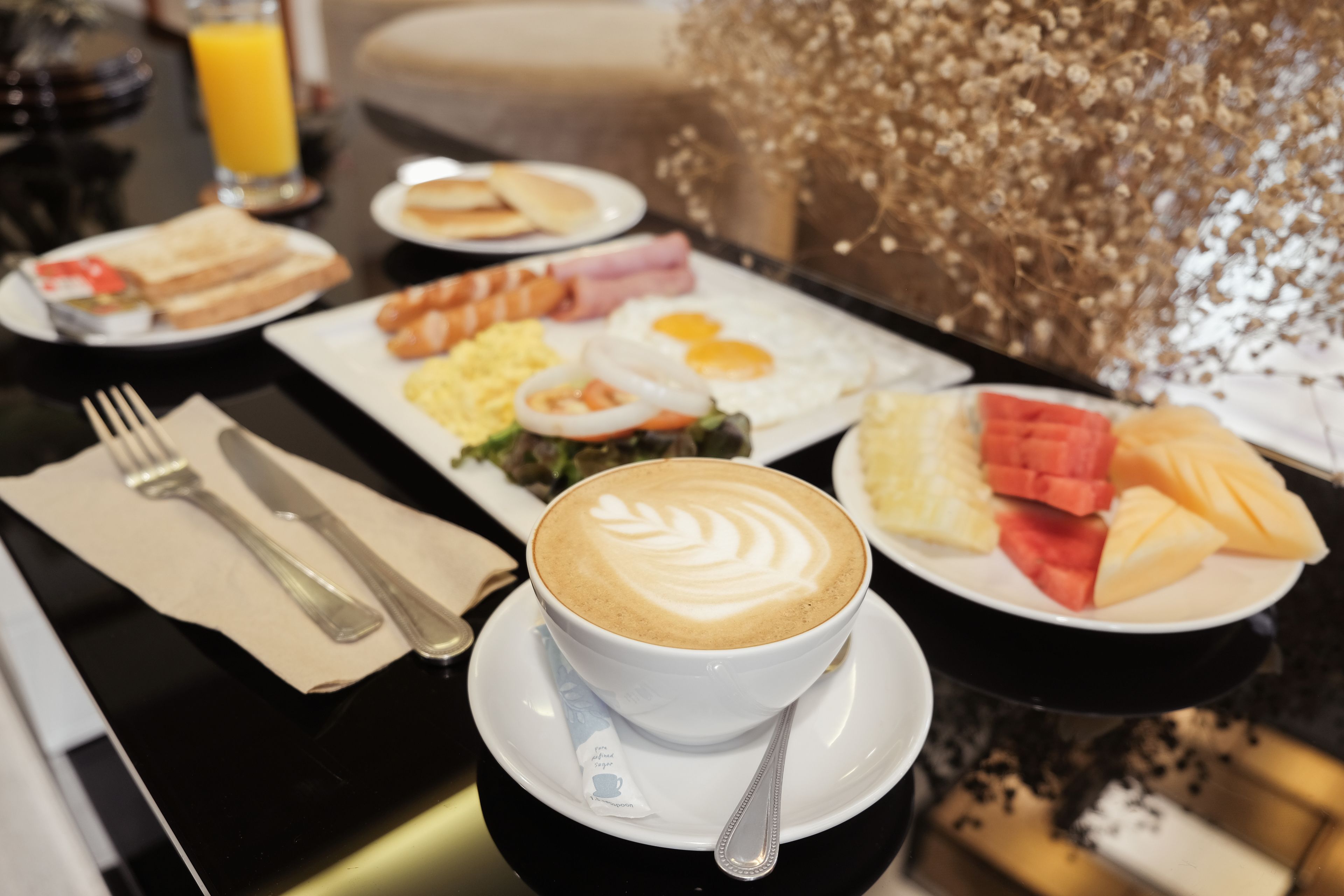 Uma mesa de café da manhã com xícara de café, pratos de ovos, torradas e frutas.