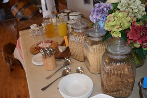 Uma mesa de jantar com diversos alimentos, utensílios e um vaso de flores.