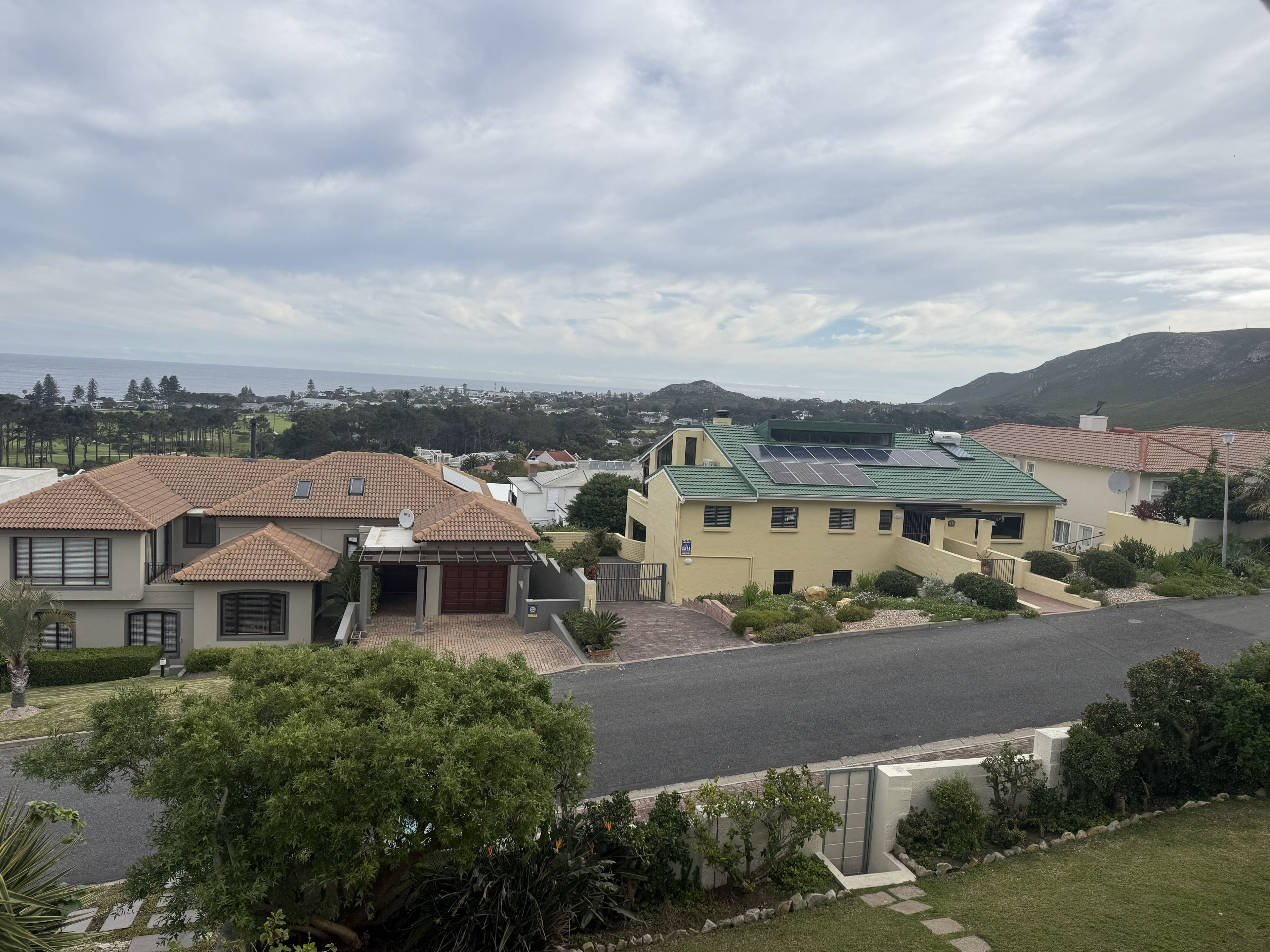 Bairro residencial com casas equipadas com painéis solares, entrada pavimentada e vista para uma paisagem montanhosa.