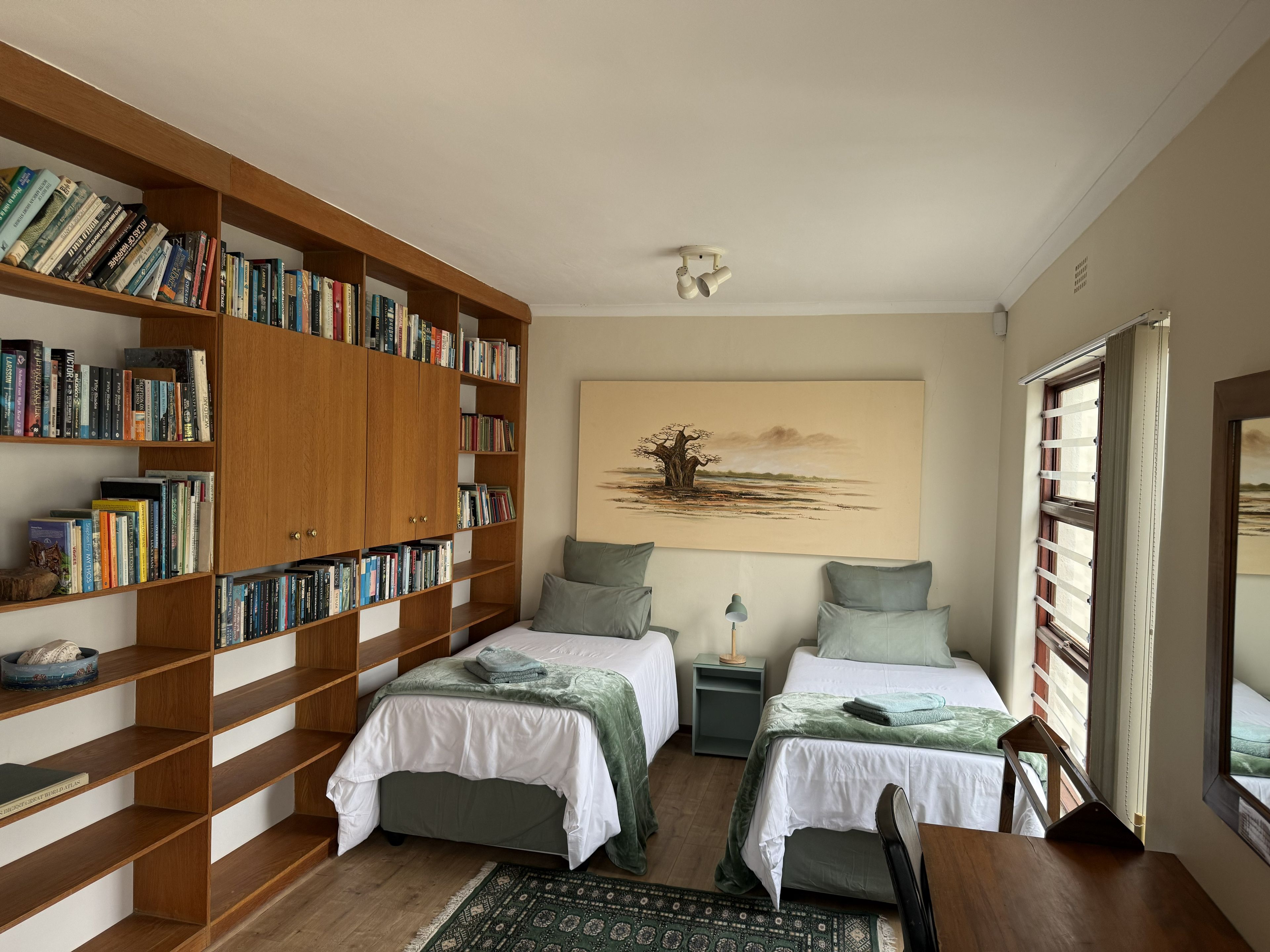 Quarto com duas camas, uma estante, um quadro e uma janela.