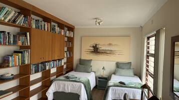 Quarto com duas camas, uma estante, um quadro e uma janela.