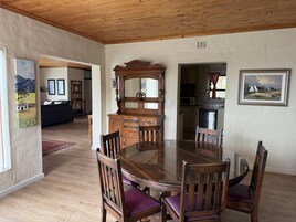 Uma área de refeições com uma mesa e cadeiras de madeira, um armário de madeira com espelho e uma cozinha ao fundo.