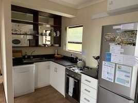 Cozinha compacta com forno embutido, micro-ondas e frigorífico. Janela proporciona luz natural e vista para o exterior arborizado.