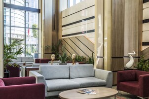 Um lobby moderno com um sofá cinzento, poltronas vermelhas e uma mesa redonda de madeira.