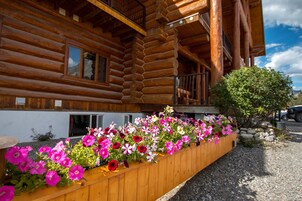 Uma cabana de madeira com varanda e um canteiro de flores rosa e vermelhas.
