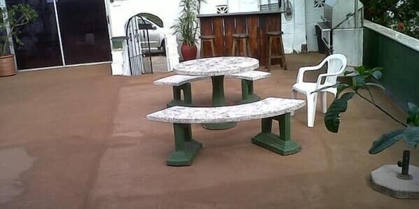 Uma área de pátio com duas mesas e cadeiras de tampo em mármore, um vaso de planta e um cercado de madeira.