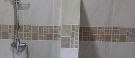Casa de banho com chuveiro, sanita e paredes revestidas a mosaico.