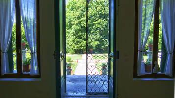 Uma porta que dá para uma varanda com grade de metal, ladeada por janelas com cortinas.