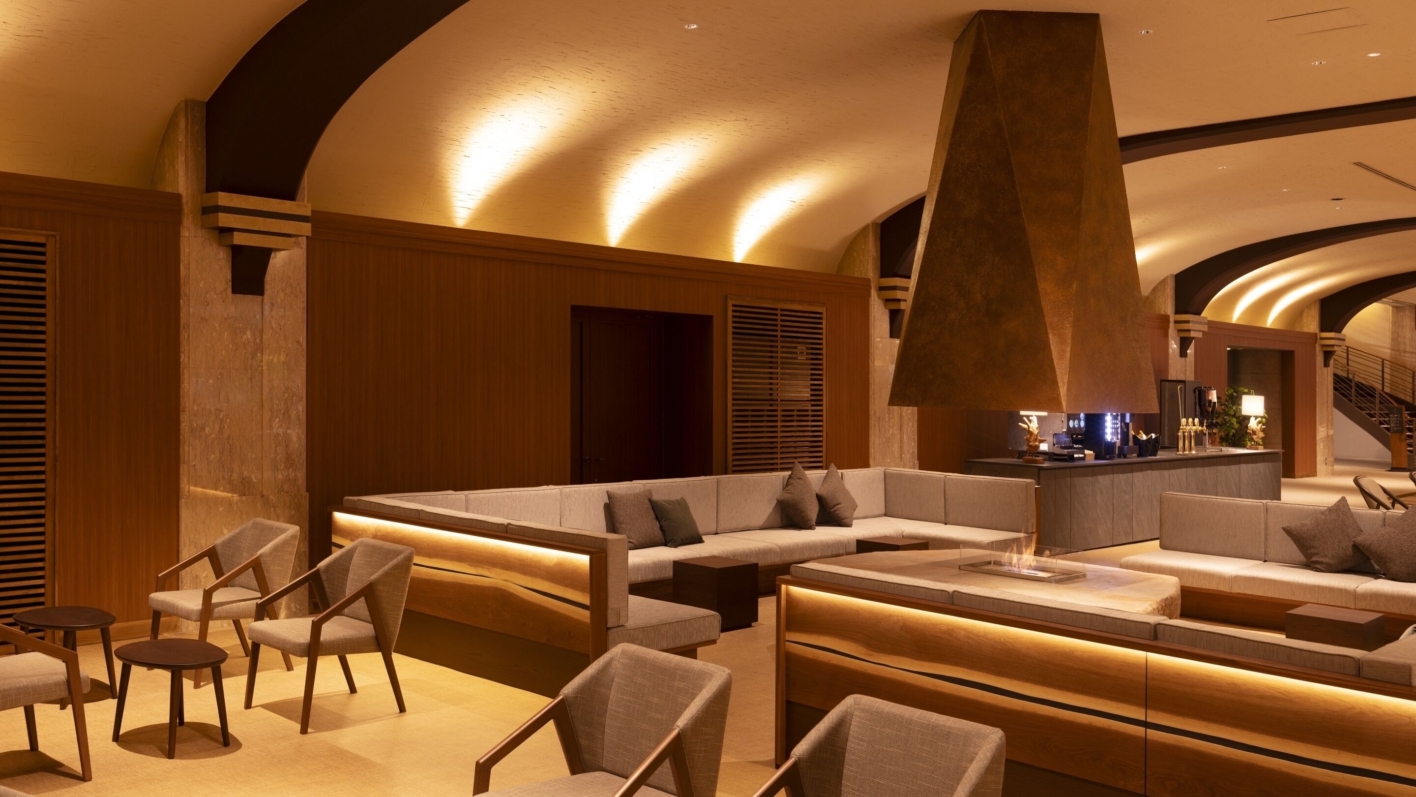 Uma área de estar moderna com um amplo sofá de canto, várias poltronas, uma mesa de centro e um espaço bar com balcão e banquetas.