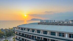 Um hotel com um letreiro no terraço com a inscrição "MICHELL", com vista para o pôr do sol sobre o mar.