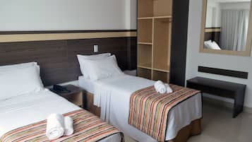 Quarto de hotel com duas camas, um guarda-roupa, uma mesa de cabeceira com telefone e um espelho na parede.