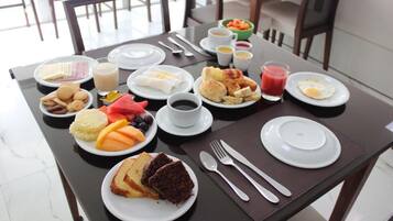 Mesa de café da manhã posta com diversos pratos, incluindo ovos, torradas, frutas e bebidas.