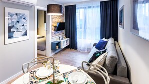 Uma sala de estar moderna com área de jantar, sofá, televisão e parede de destaque em tijolo.