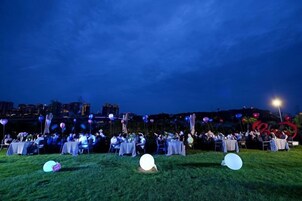 Evento ao ar livre com mesas montadas em área gramada, sob um céu noturno.
