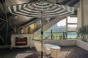 Quarto com teto inclinado, rede, lareira, ampla janela com vista e um guarda-sol listrado.