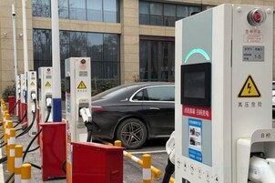 Estações de carregamento para veículos elétricos, com um carro estacionado por perto, um edifício ao fundo e placas de aviso de segurança.