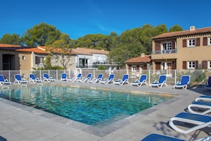Uma piscina com espreguiçadeiras e um edifício com telhado em azulejo.