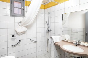 Casa de banho com paredes revestidas de azulejos brancos, uma pia bege, um espelho, chuveiro com acessório de duche manual e uma cortina.
