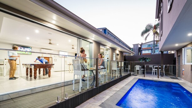 Uma área de piscina interna moderna, com guarda-corpos de vidro, mesa de bilhar e espaços para relaxar.