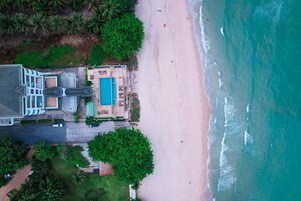 Vista aérea de uma propriedade à beira-mar com piscina, uma casa grande e a praia.