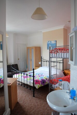 Quarto com beliches, mesa de cabeceira, guarda-roupa de madeira, espelho e banheiro com pia.