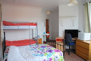 Quarto com beliches, escrivaninha, cadeira, televisão e janela com cortinas.