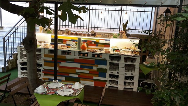 Uma exibição colorida de alimentos com diversos doces e bebidas, emoldurada por uma estrutura de madeira rústica e plantas em vasos.