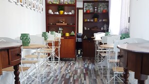 Quarto com piso de madeira estampado, cadeiras brancas, mesa de madeira e uma estante com diversos objetos.