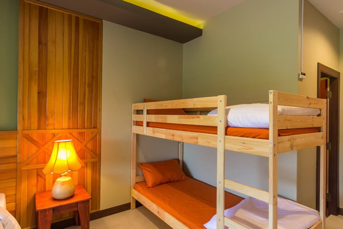 Quarto com beliche, cabeceira de madeira, mesinha de cabeceira com luminária e painel na parede.