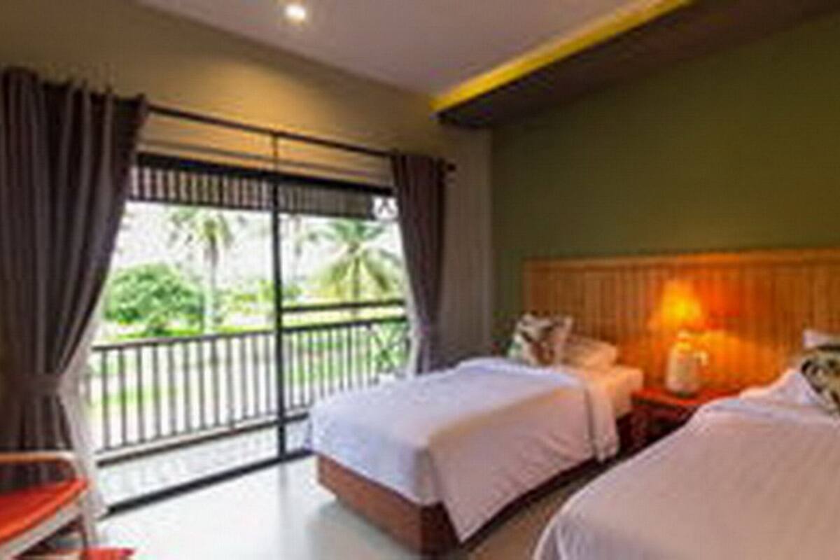 Quarto de hotel com duas camas, uma mesinha de cabeceira e vista para o verde através de uma porta de correr.