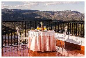 Mesa com toalha e duas cadeiras numa varanda com vista para as montanhas.