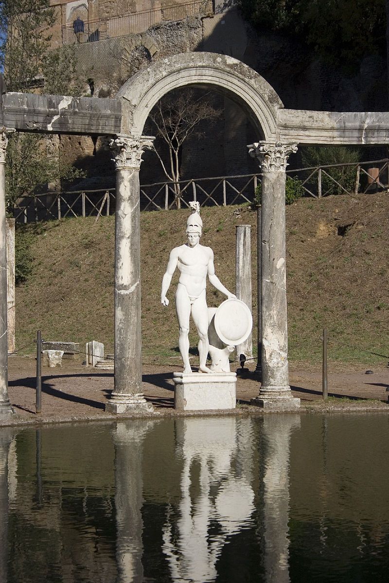 Estátua de figura clássica em um espelho d'água, rodeada por colunas e um arco de estilo clássico.